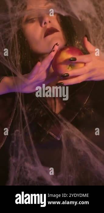 A mysterious witch casts spells while holding a red apple, her ...