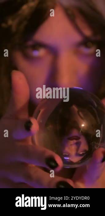A witch moves her hands around a crystal ball as if casting a spell. The close-up video captures ...