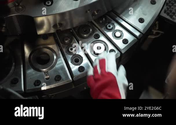A worker's hands in red and white gloves operate a precision machine ...