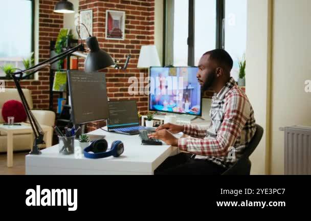 Male coder works from home typing code on a laptop in a modern living room. African american IT ...
