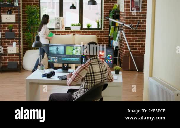 African american freelancer editing a background video at his home office, mixing clips on dual ...