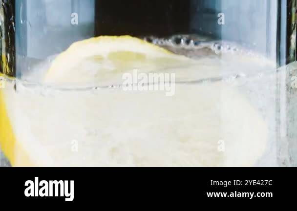 A lemon slice is dropped into sparkling water, creating an explosion of bubbles that rise ...