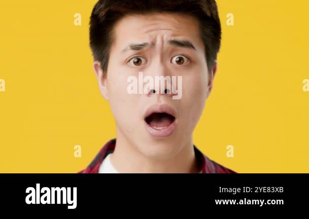 Asian young man displays an expression of shock and surprise, with his mouth open and eyes wide ...