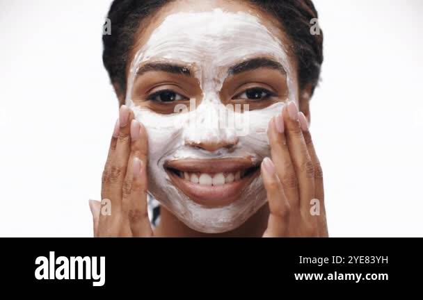 African American woman applies a creamy facial mask to her face while ...