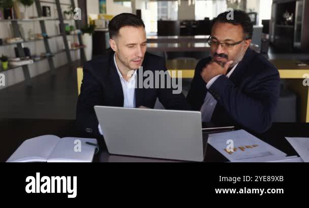 Two multiethnic businessmen negotiate in office, sit at desk with ...