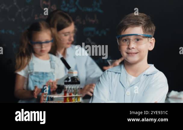 Smart boy crossing arms while teacher and friend doing experiment at ...