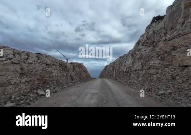 Driving through the gravel road cut from rocks on a mountain top wind ...