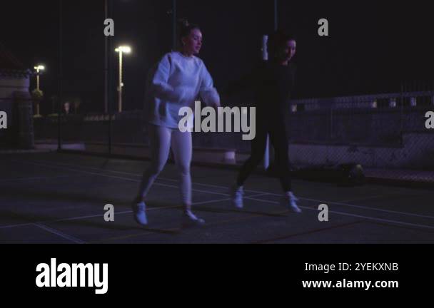 Two women engage in a dynamic workout outdoors at night, showcasing ...