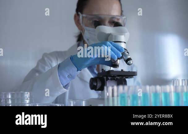 Scientist woman, wearing a lab coat, mask, blue gloves and safety glasses, is adjusting a ...