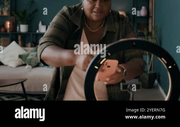 Senior Black woman placing her smartphone at ring led lamp holder and ...