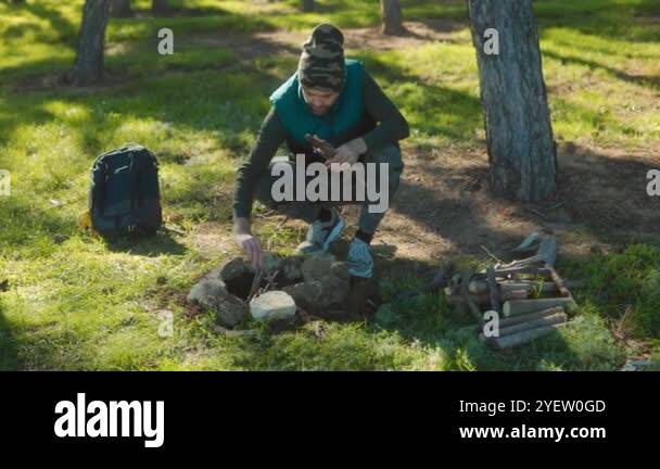 In the heart of nature, a man prepares a campfire by adding wood ...