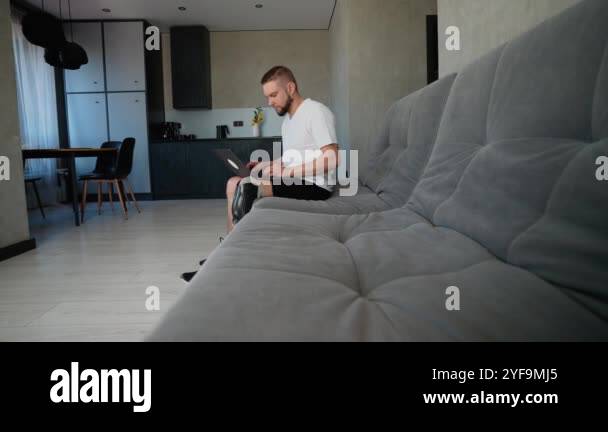 A programmer with a prosthetic leg works remotely from home, focused on his laptop while sitting ...