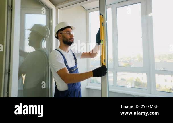 Professional construction worker in safety gear uses a spirit level to align a window frame ...