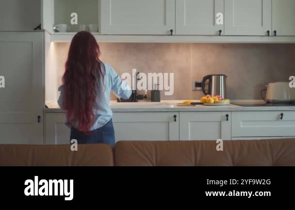 A woman with long hair prepares food at a modern kitchen counter, under ...