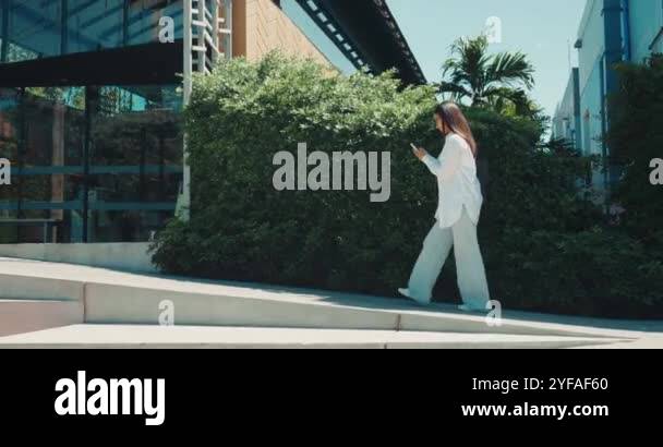 Woman walking down street using phone smiling with joy reflects simple ...