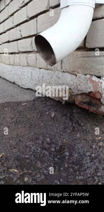 Water drain on the facade of a brick building. Rainwater flows from the roof onto the asphalt ...
