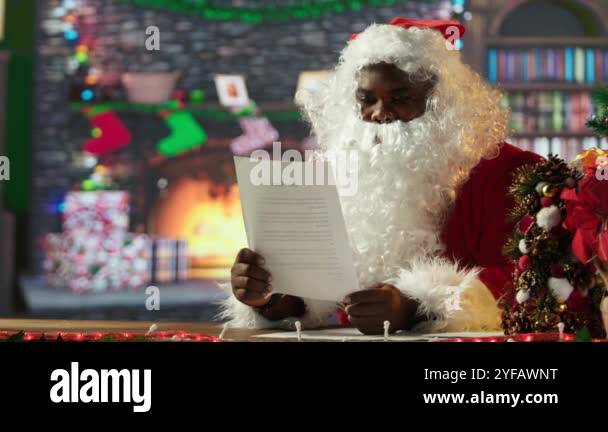Santa Claus reads a Christmas letter by the fireplace in his workshop ...