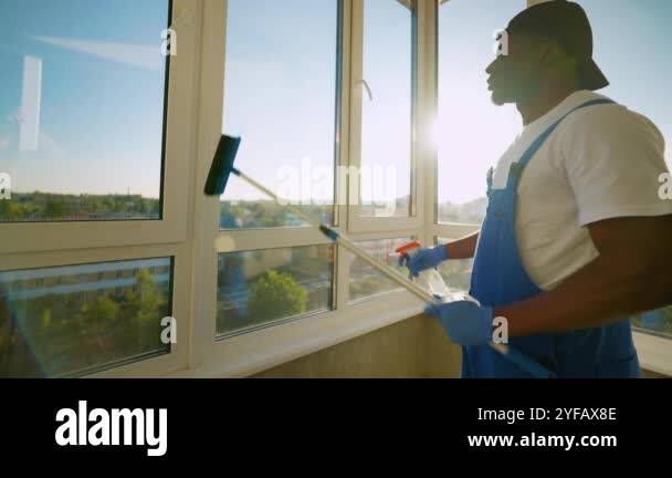 African American man in blue overalls and gloves sprays cleaner on a ...