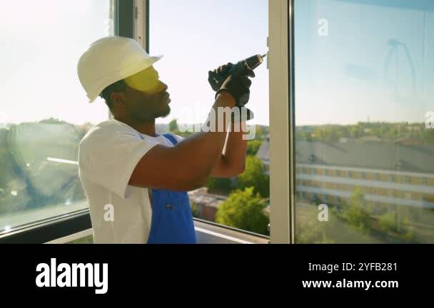 A skilled technician in safety gear installs a PVC window using a power ...