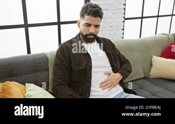 Young latin man suffering from painful stomachache at home, hand on his ...