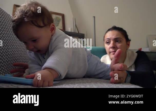 Baby lying on couch holding blue object while mother supports, baby ...