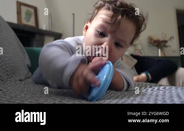 Baby playing with blue object while leaning on couch, mother watching ...