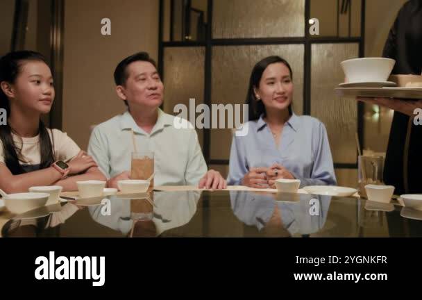 Wide shot of Asian family of daughter, father and mother looking at waiter serving their table ...