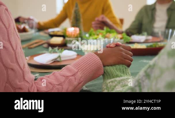 At Christmas, diverse friends holding hands around festive table ...