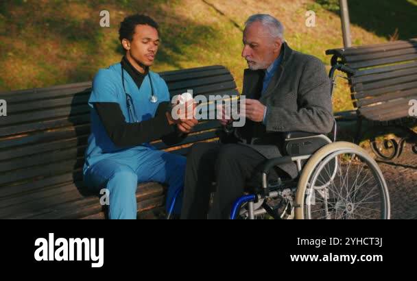 Hispanic doctor taking care of old disabled friend in wheelchair. Latin ...