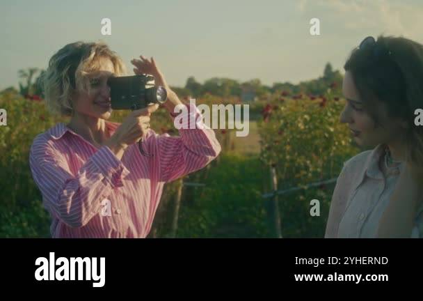 Girl cameraman filming her friend in a flower garden on a vintage super ...