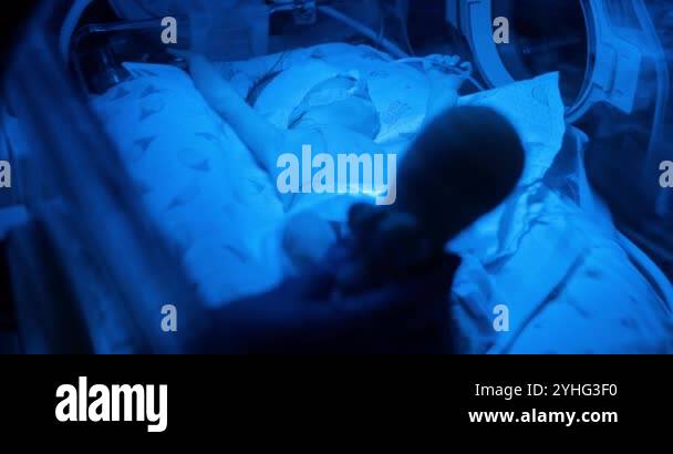A newborn baby is placed in an incubator where it is receiving blue ...