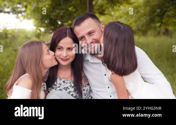 Two pretty sisters kissing their father and mother during summer picnic ...