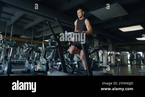 Focused young male athlete using a treadmill in a well-equipped, spacious gym. Captures the ...