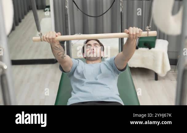 Man performing seated core exercise on pilates trapeze holding bar to ...