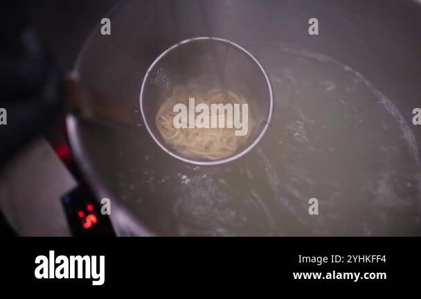Close-up of freshly cooked noodles being lifted from boiling water with ...