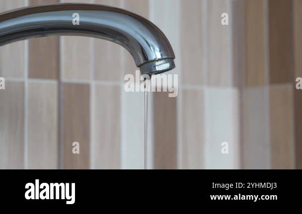 Water flows in a thin stream from the tap in kitchen. From the tap is ...