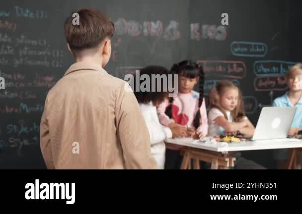 Smart boy smiling at camera while diverse friend working or learning engineering code or prompt ...