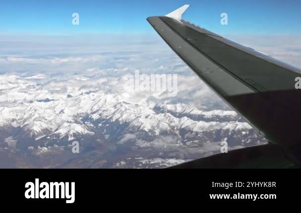 Plane wing through an airplane window in flight trip, snow capped Alps ...
