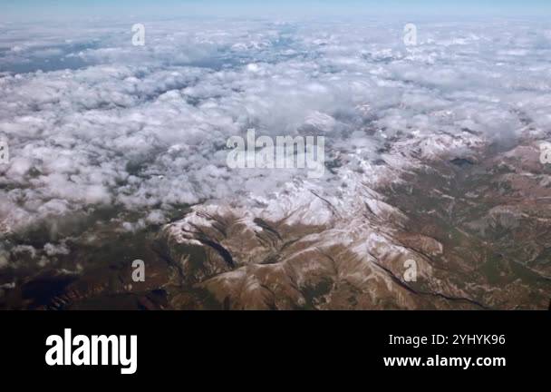 Above the peaks with clouds, capped Alps with rugged mountain peaks extending across the ...