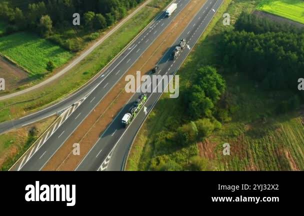 Trucks loaded with cars move along rural four-lane divided highway ...