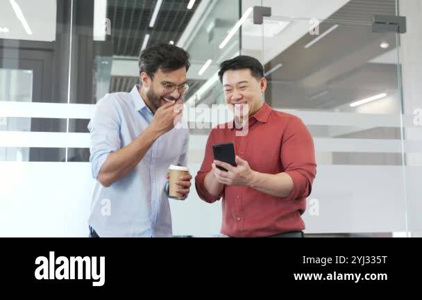 Two coworkers laughing and chatting over a phone in a modern business ...