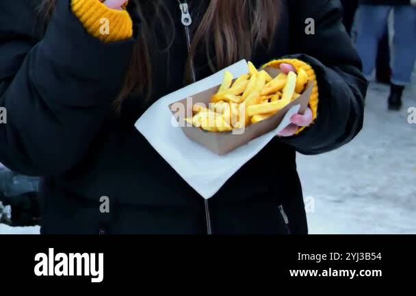 Fast food. Girl eating french fries on the street on a crowd of people ...