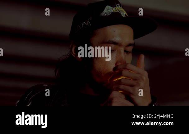 A close-up of a man with long hair wearing a cap, looking contemplative ...