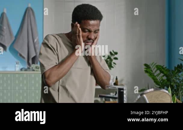 Medium shot of just woken up Black man standing at modern bathroom sink ...