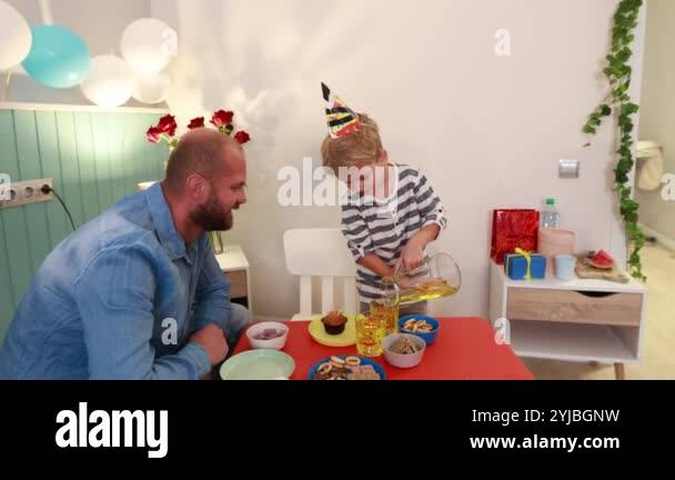 A father and son celebrate a birthday at home. The son is wearing a ...