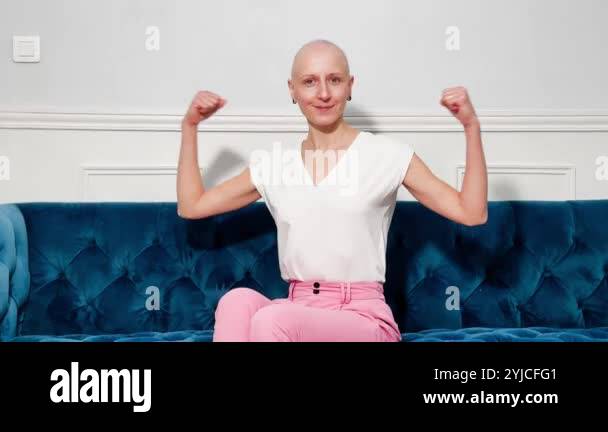 smiling bald woman showing her muscles while sitting on a navy blue ...