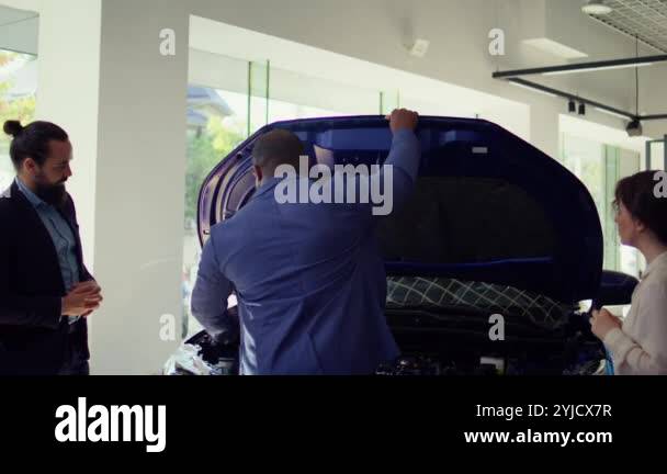 Customers in car showroom looking at components under vehicle hood ...