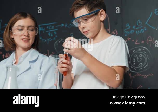 Smart boy pour chemical liquid in beaker while teacher giving advice at ...