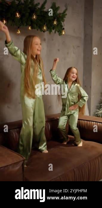 Two little girls, dressed in matching green satin pajamas, laugh and ...
