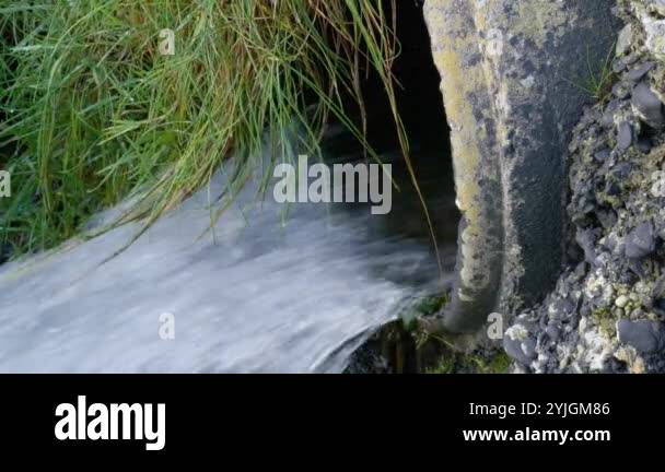 A concrete culvert with a smooth, dark surface has water flowing out of ...